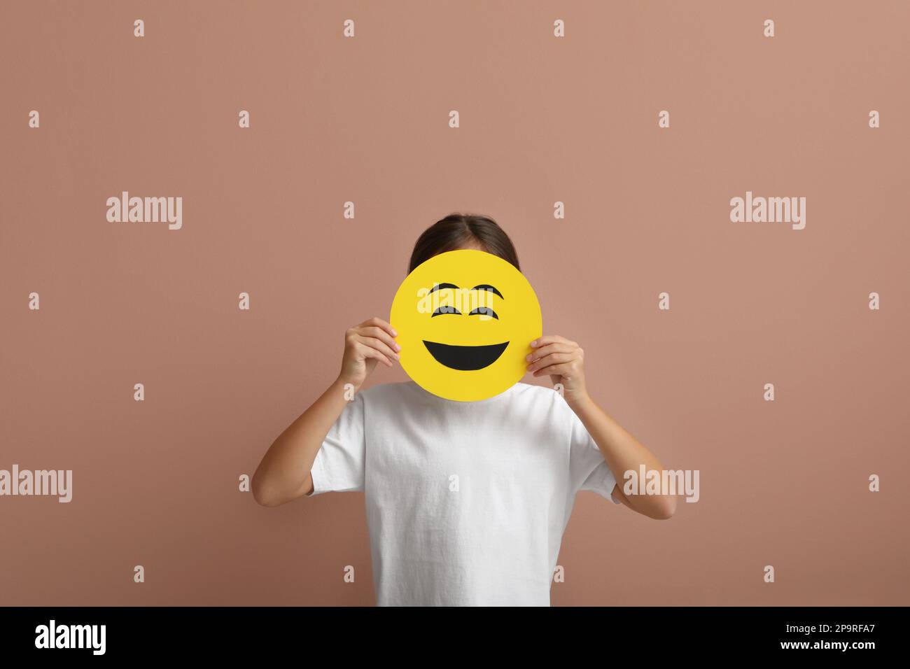 Little girl covering face with laughing emoji on pale pink background ...