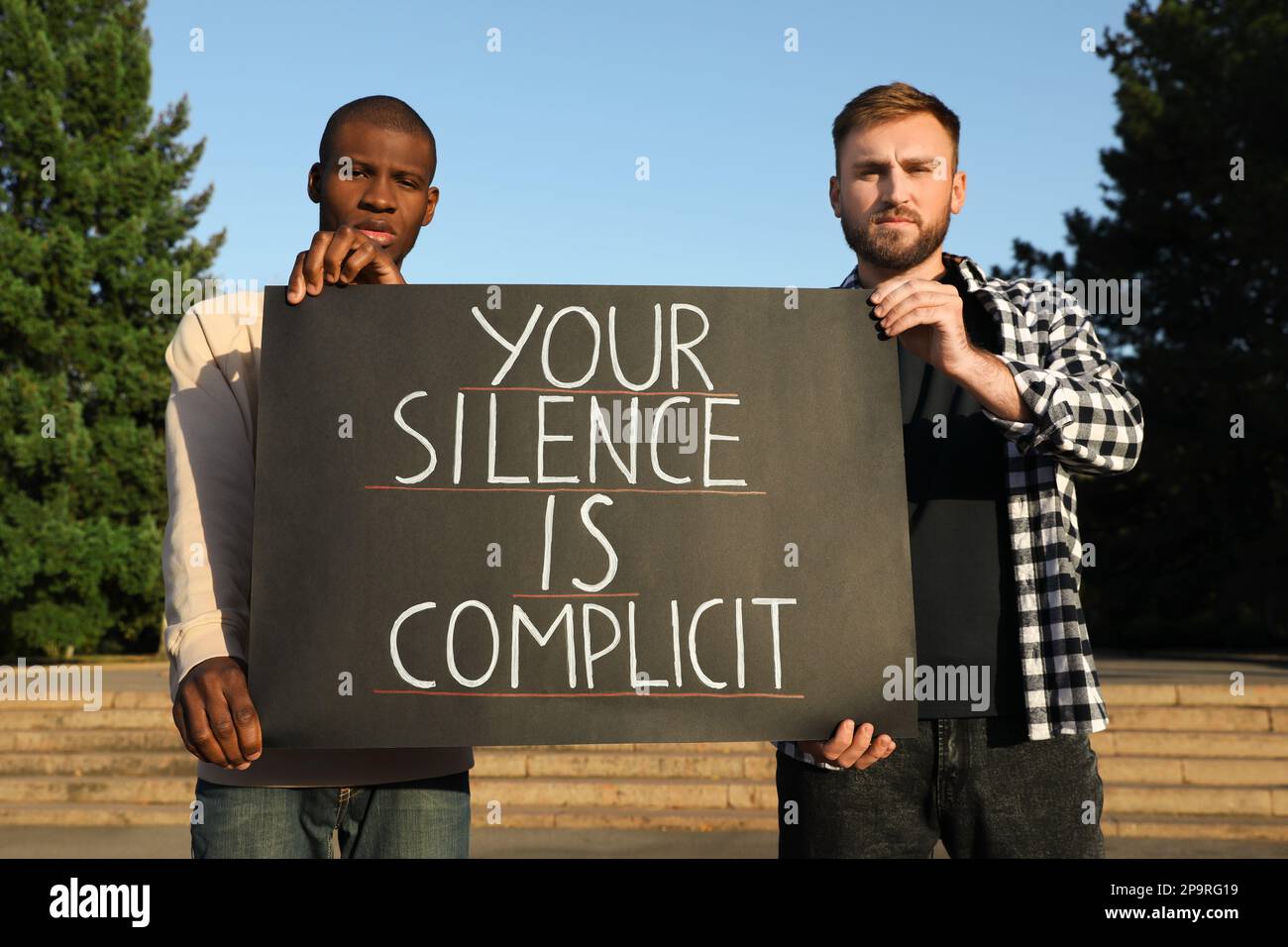 Men holding sign with phrase Your Silence Is Complicit outdoors. Racism ...