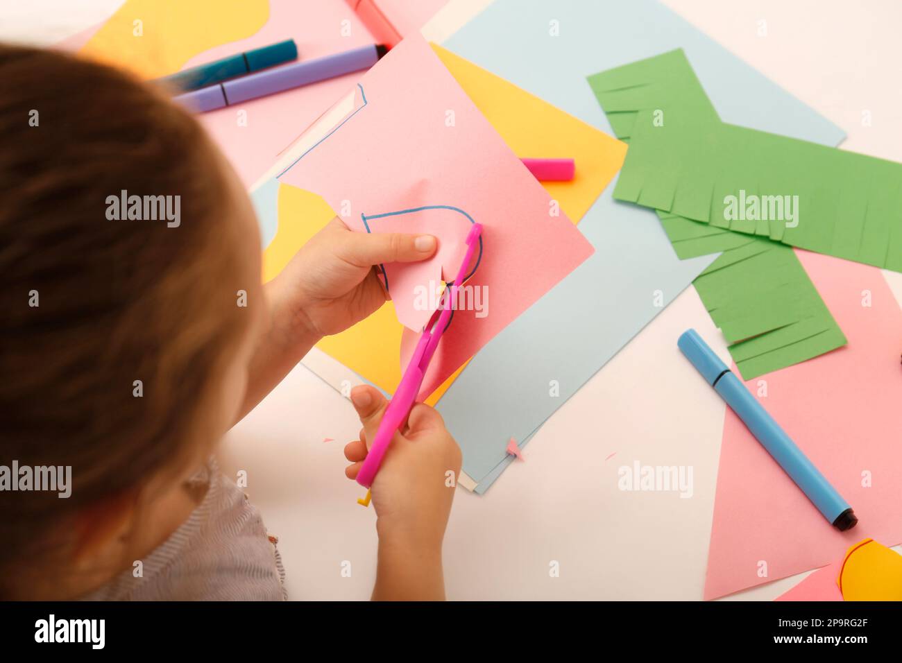 Little girl cutting color paper with scissors at table, above view ...