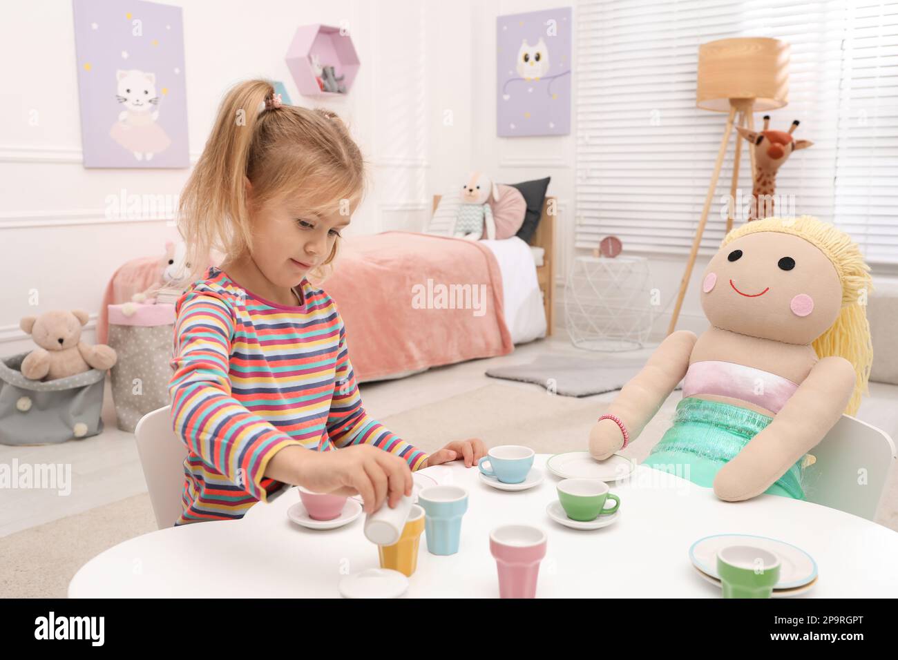 Cute little girl playing tea party with doll at table in room Stock ...