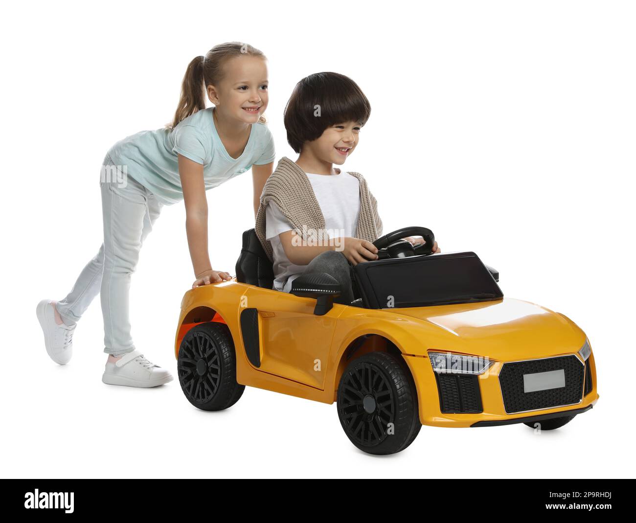 Cute girl pushing children's electric toy car with little boy on white ...