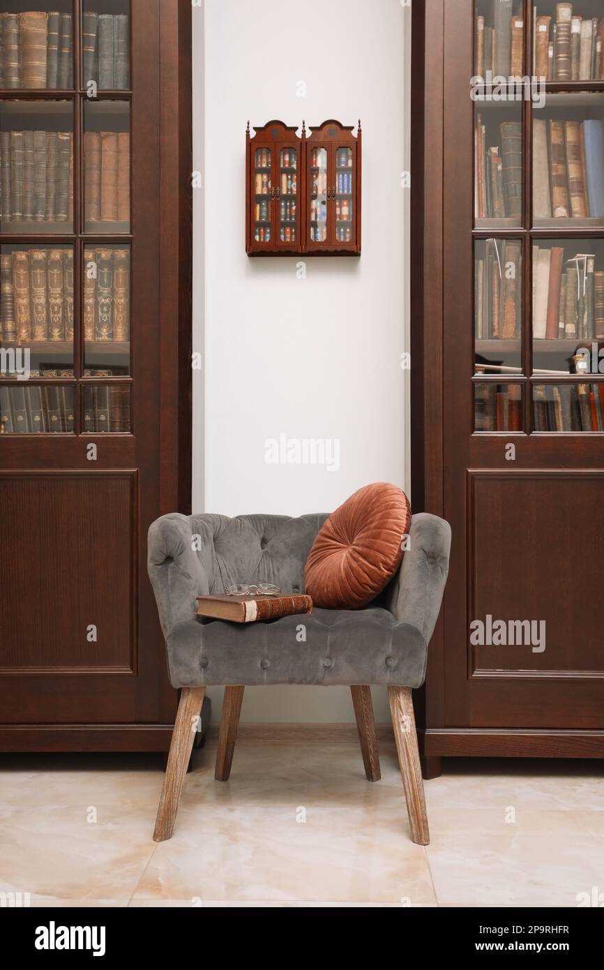Comfortable armchair with pillow and book between wooden bookcases in ...