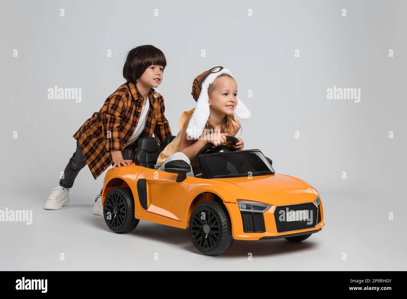 Cute boy pushing children's electric toy car with little girl on grey ...