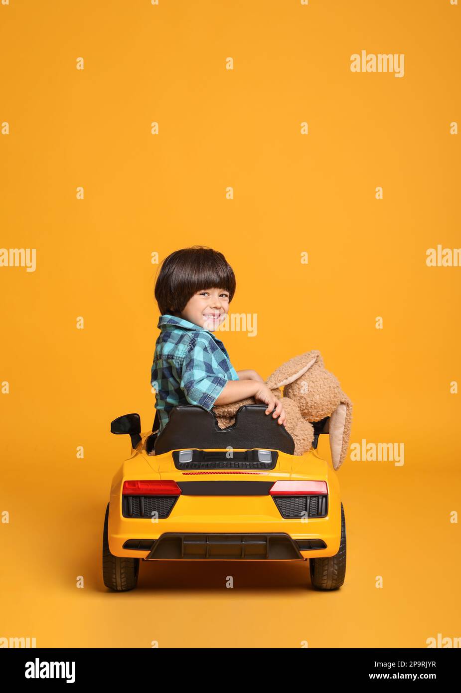 Cute little boy with toy bunny driving children's car on yellow ...