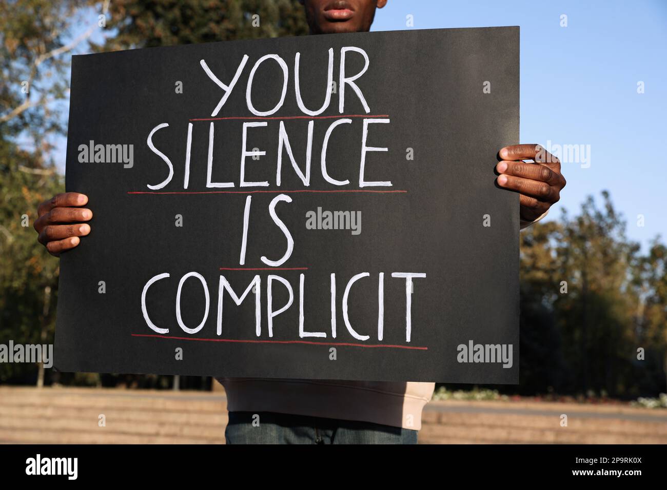 African American man holding sign with phrase Your Silence Is Complicit ...