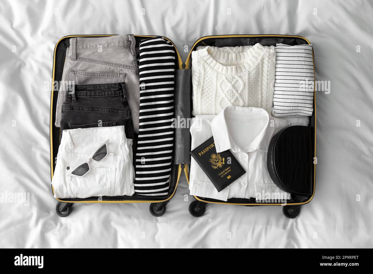 Open suitcase with clothes, passport and accessories on bed, top view ...