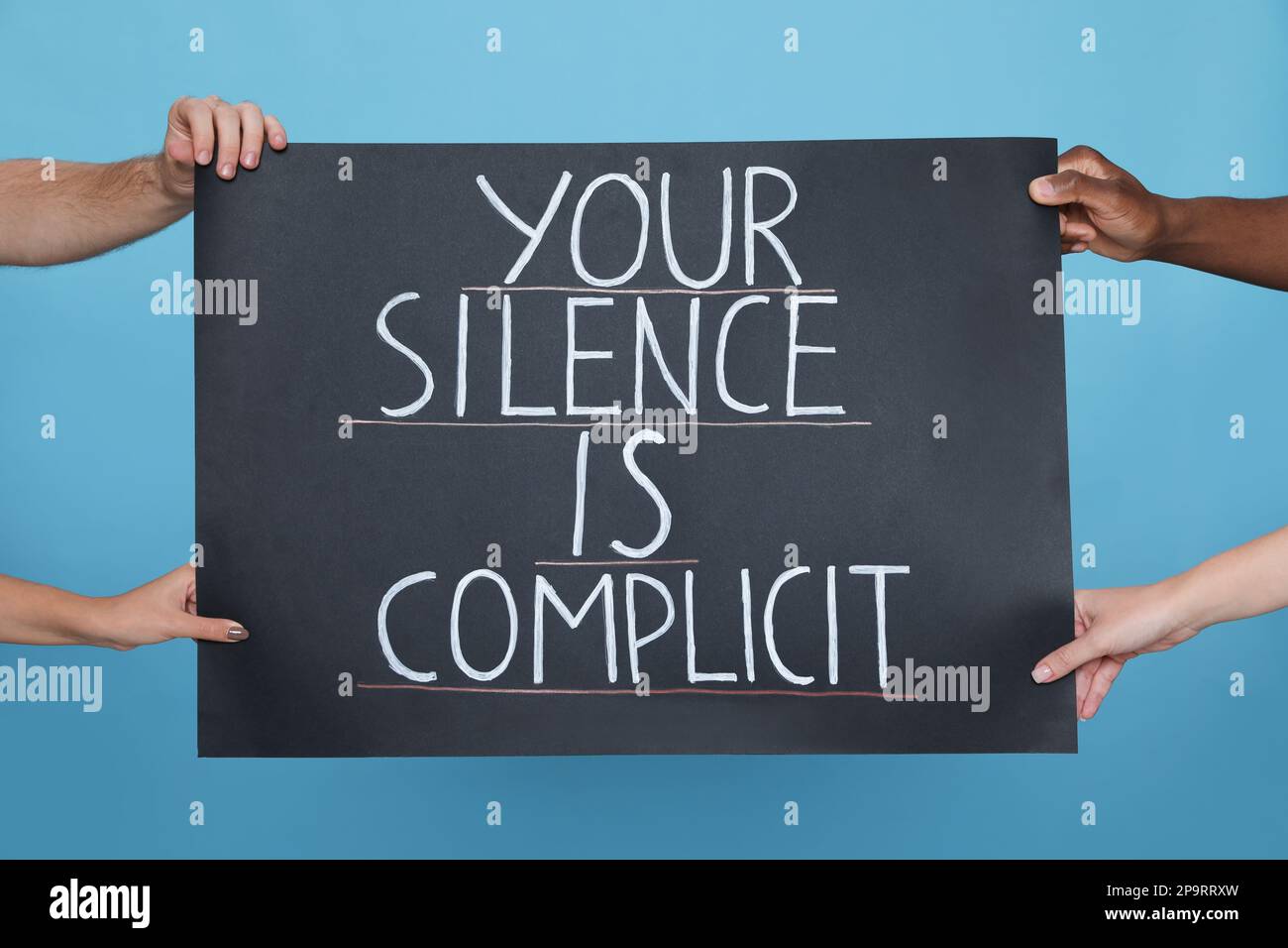 People holding sign with phrase Your Silence Is Complicit on light blue background, closeup ...