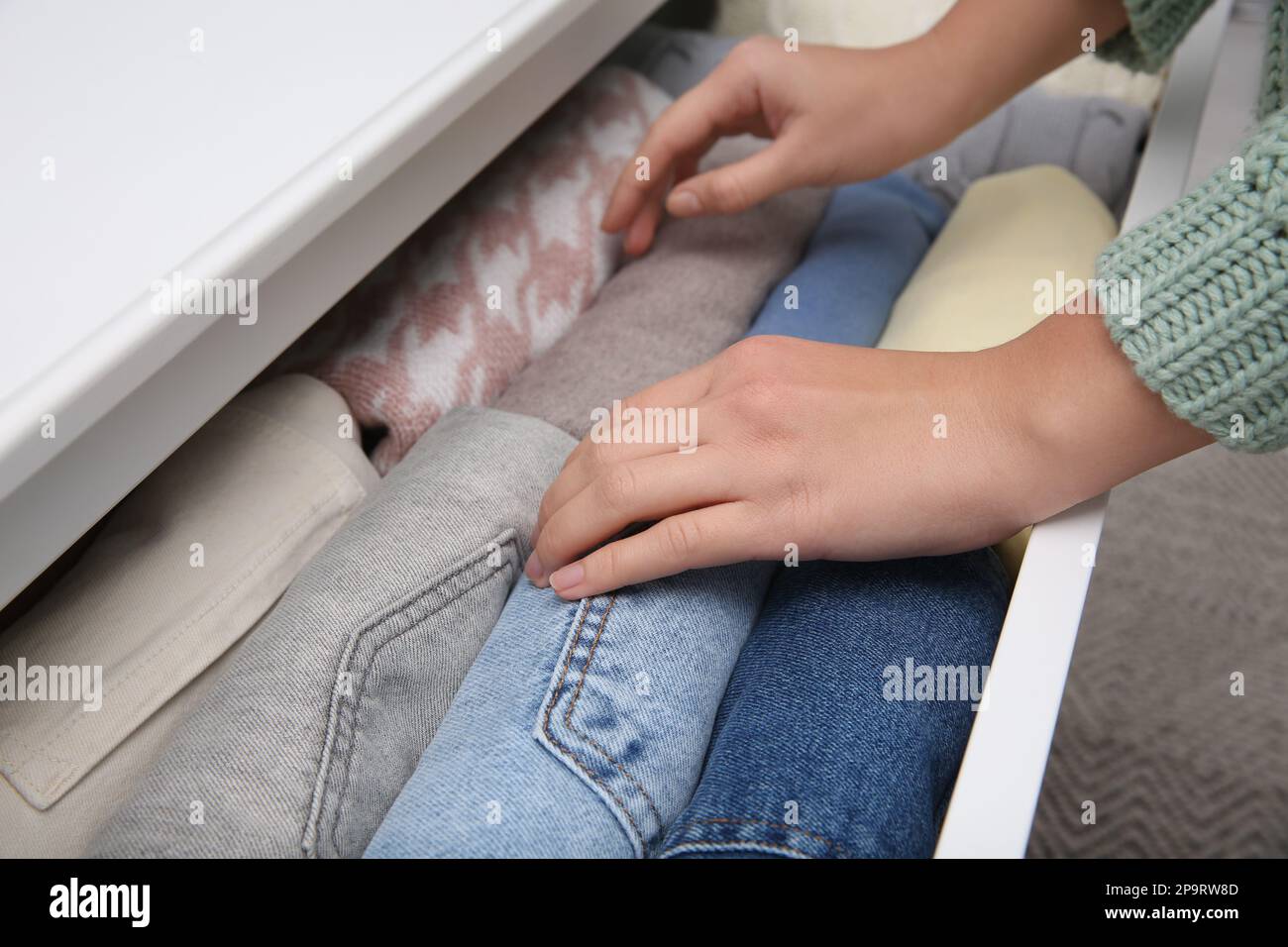 Woman putting folded clothes into drawer indoors, closeup. Vertical ...