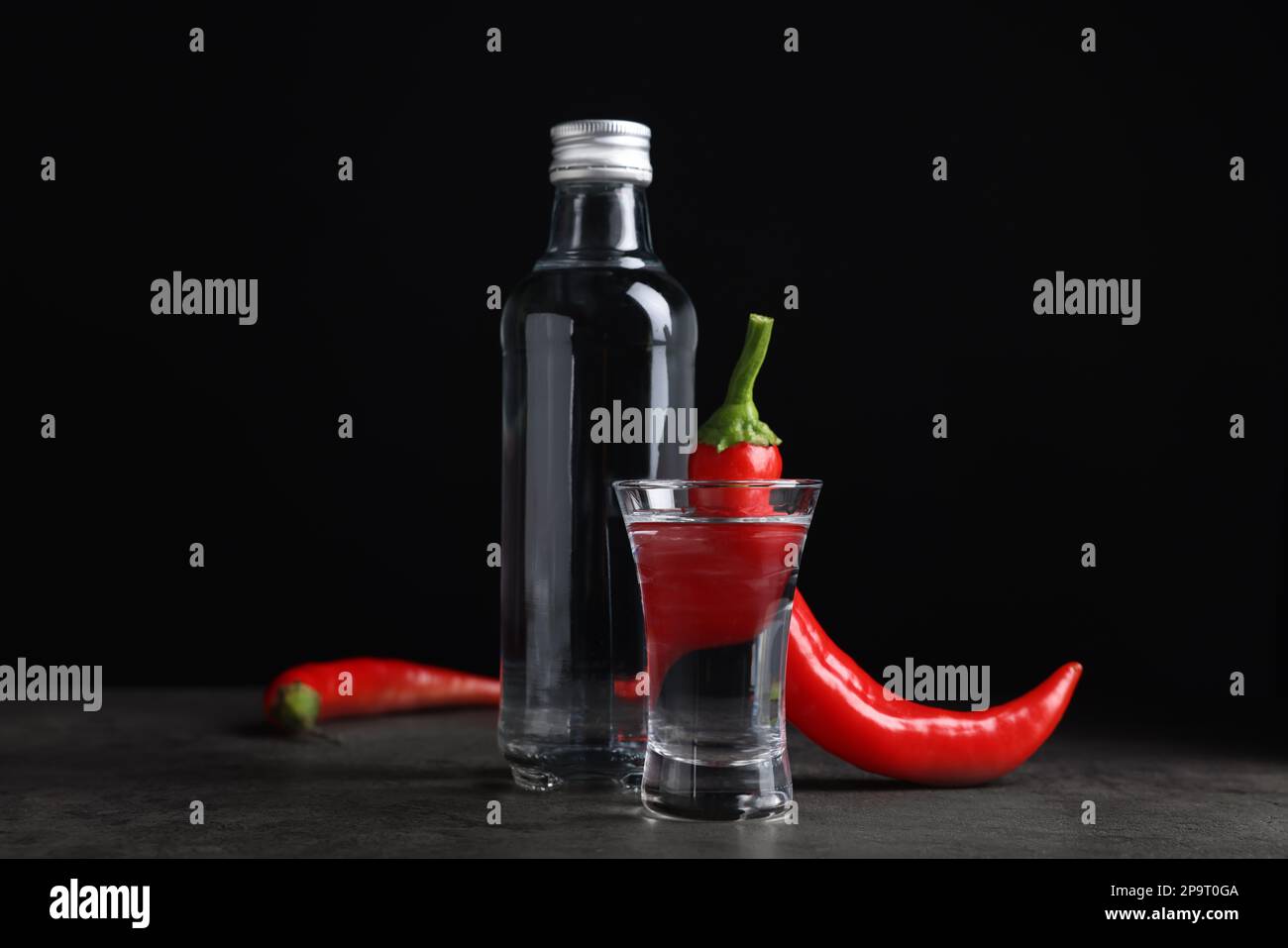 Red hot chili peppers and vodka on grey table against black background ...