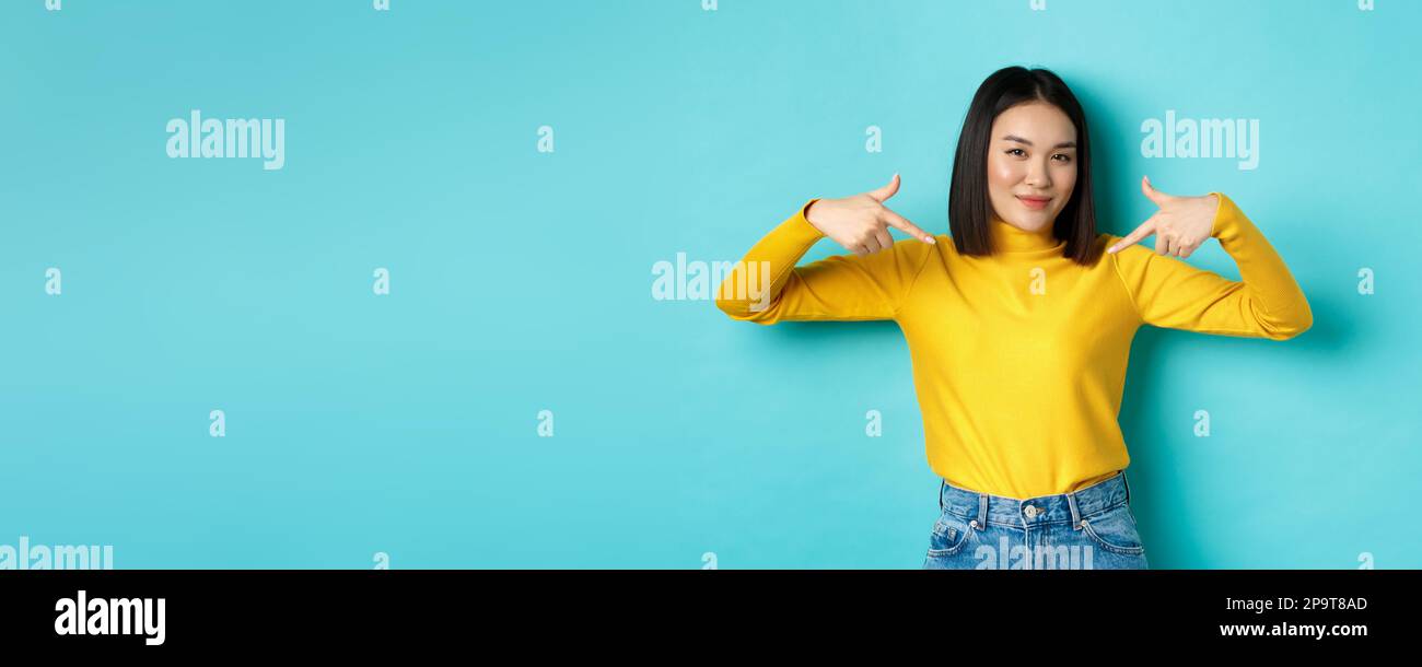 Confident asian woman in stylish sweater pointing fingers at logo on ...