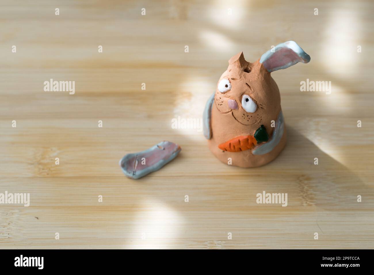 Clay Bunny with Broken Ear Holds Carrot, Standing on Sunlit Wooden ...