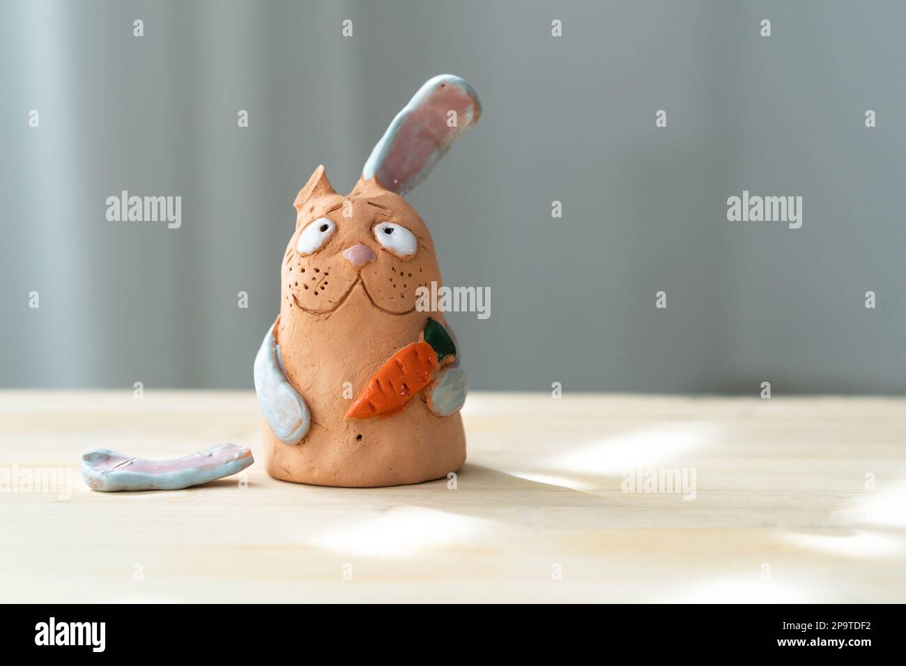 Sad Clay Rabbit with Broken Ear Holds Carrot and Looks at Camera. Hand ...