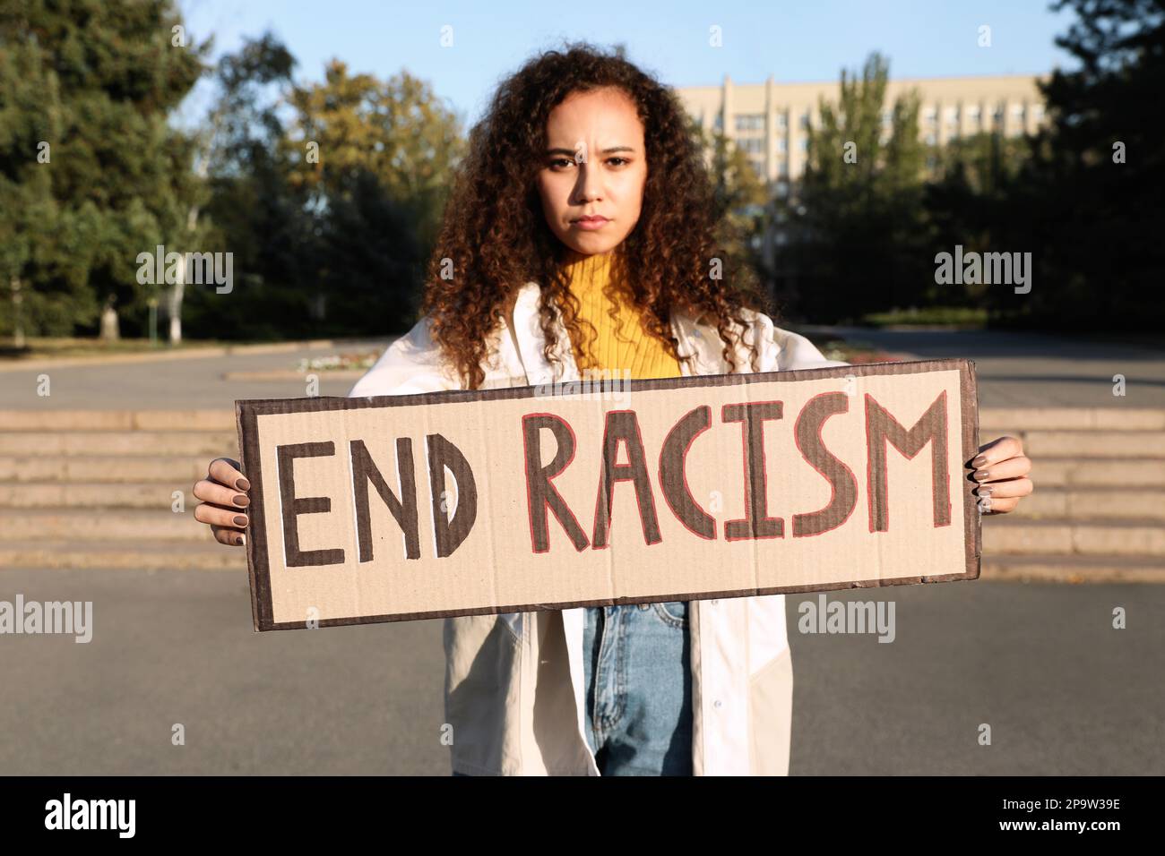 African American woman holding sign with phrase End Racism outdoors ...