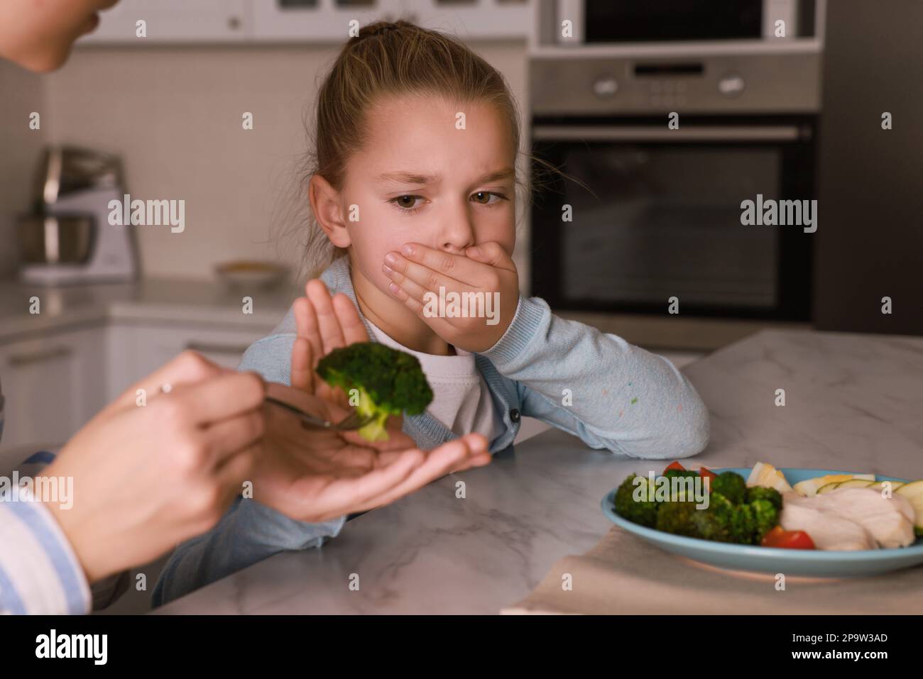 Mother feeding her daughter in kitchen, closeup. Little girl refusing ...