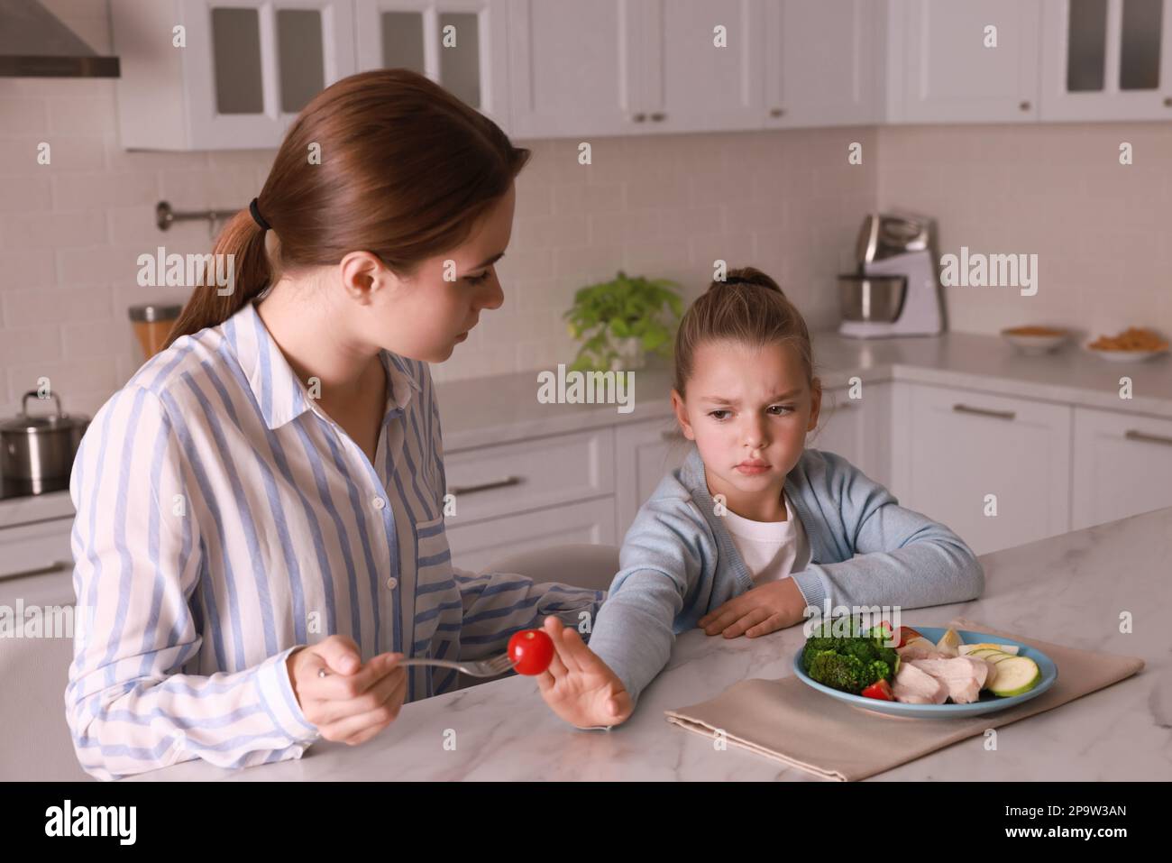 Mother feeding her daughter in kitchen. Little girl refusing to eat ...