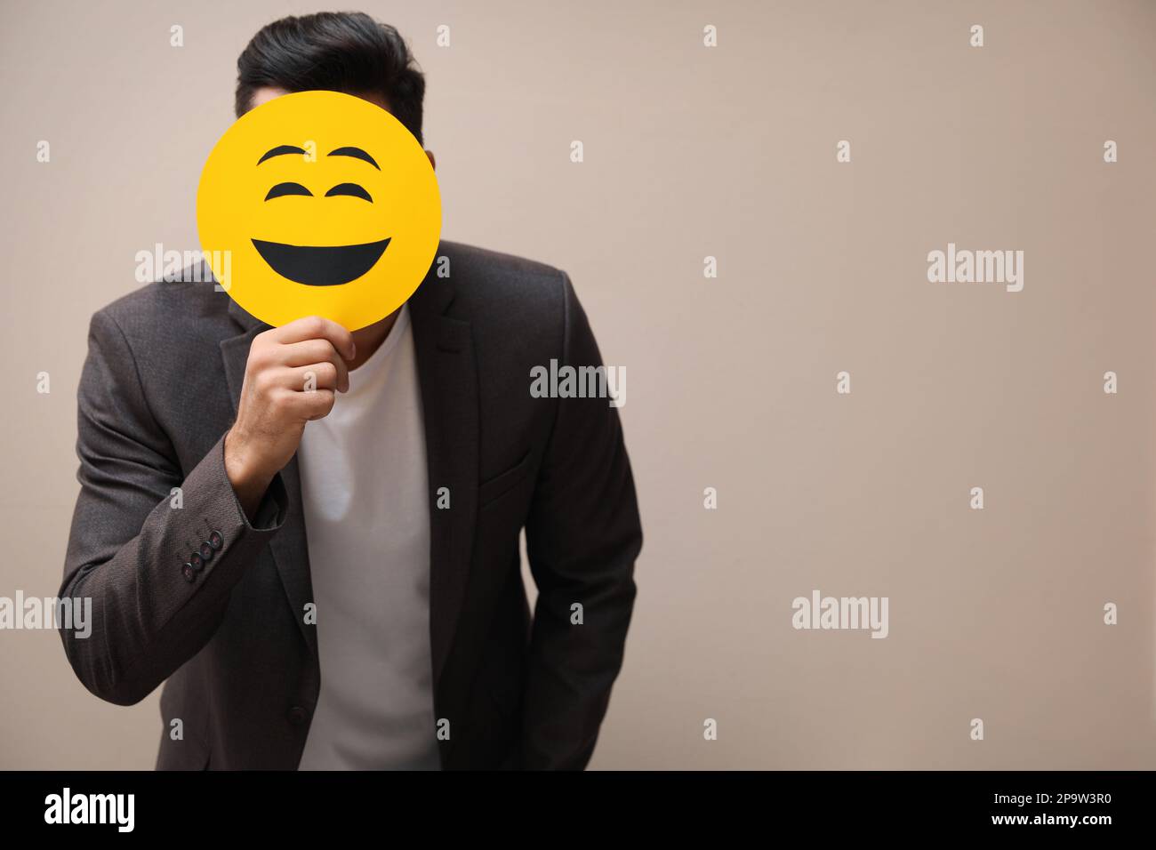 Man hiding emotions using card with drawn smiling face on beige ...