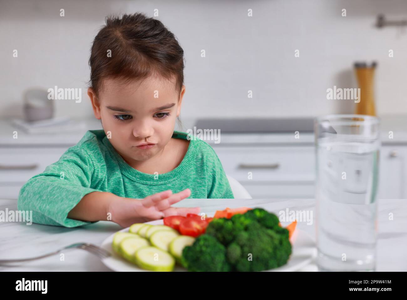 Cute little girl refusing to eat vegetables in kitchen Stock Photo - Alamy