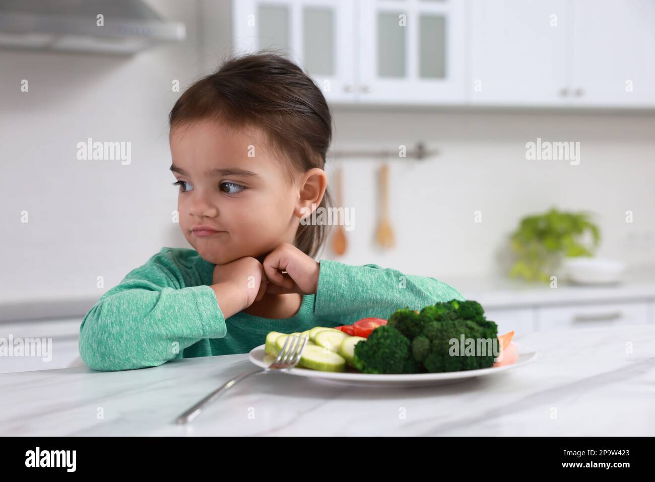 Cute little girl refusing to eat vegetables in kitchen Stock Photo - Alamy