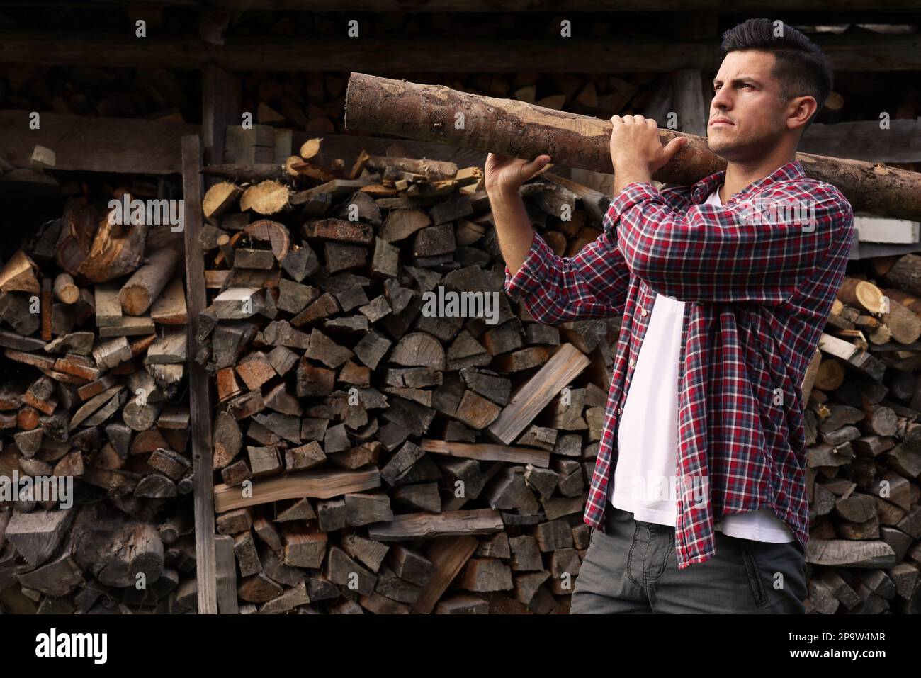 Man with log near wood pile outdoors Stock Photo - Alamy