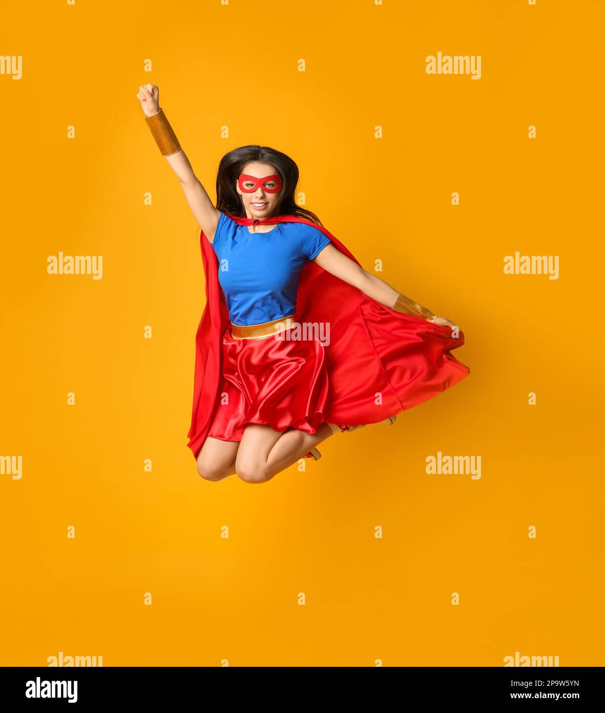 Confident young woman in superhero costume jumping on orange background ...