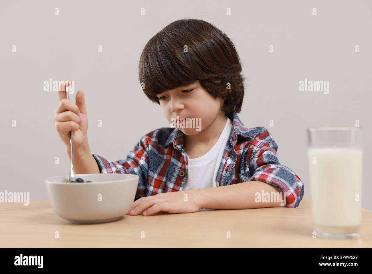 Cute little boy refusing to eat his breakfast at table on grey ...