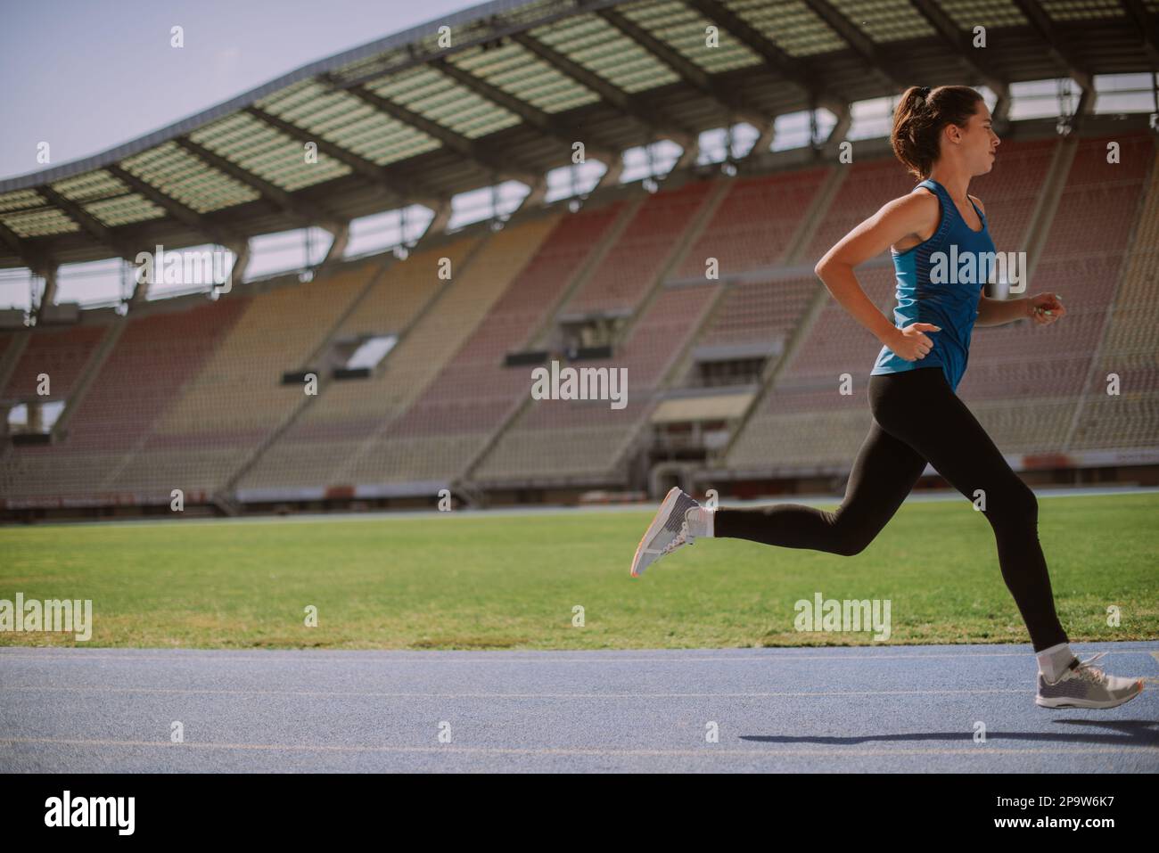 An attractive 20s girl is jogging around the stadium, on a sports track ...