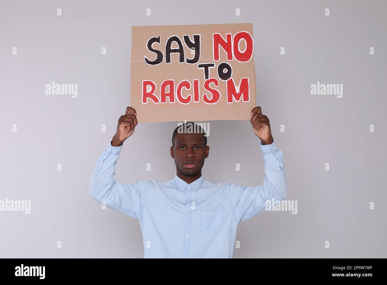 African American man holding sign with phrase Say No To Racism on light ...
