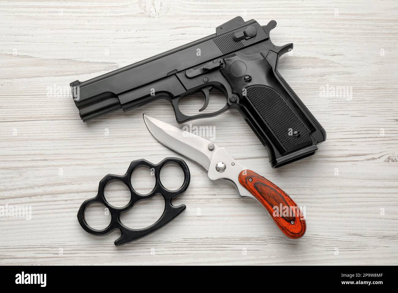 Black brass knuckles, gun and knife on white wooden background, flat ...