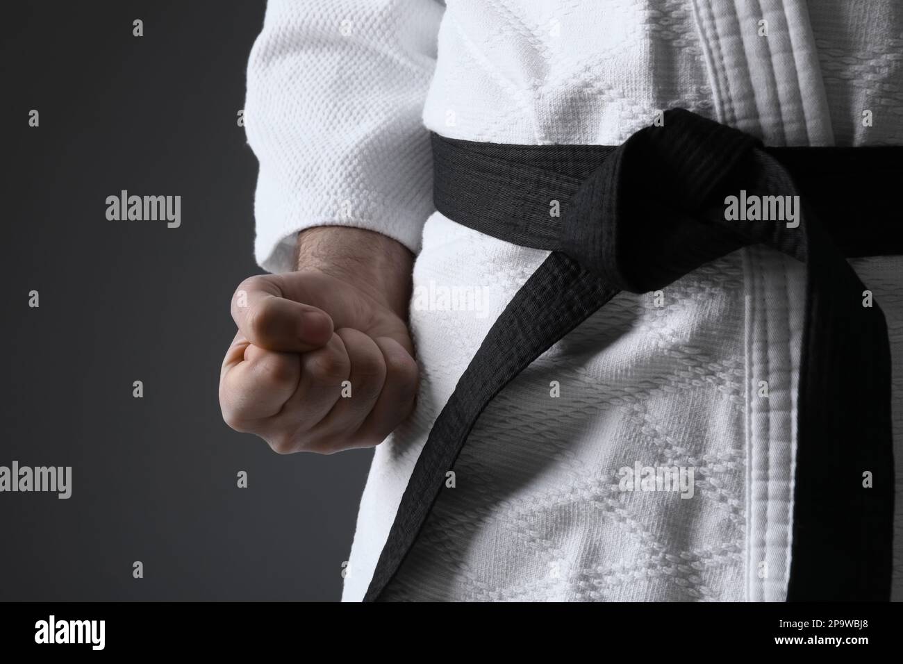 Karate coach wearing kimono and black belt on grey background, closeup ...