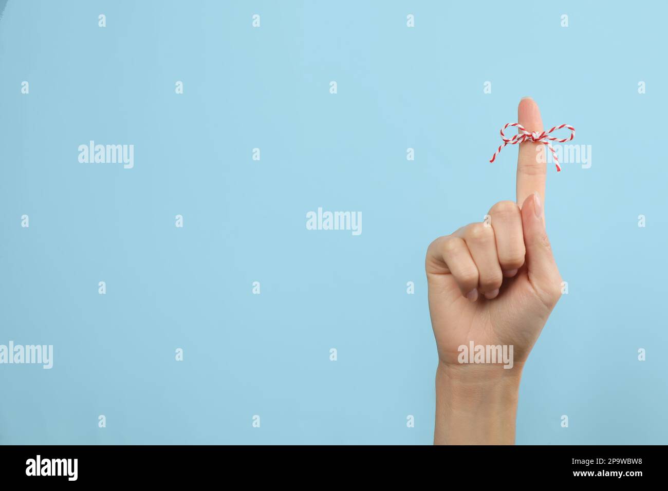 Woman showing index finger with tied bow as reminder on light blue ...