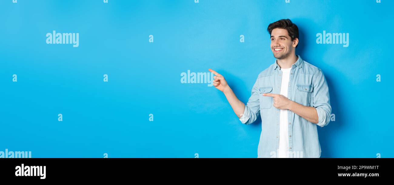 Handsome adult man introduce product, looking and pointing fingers left ...