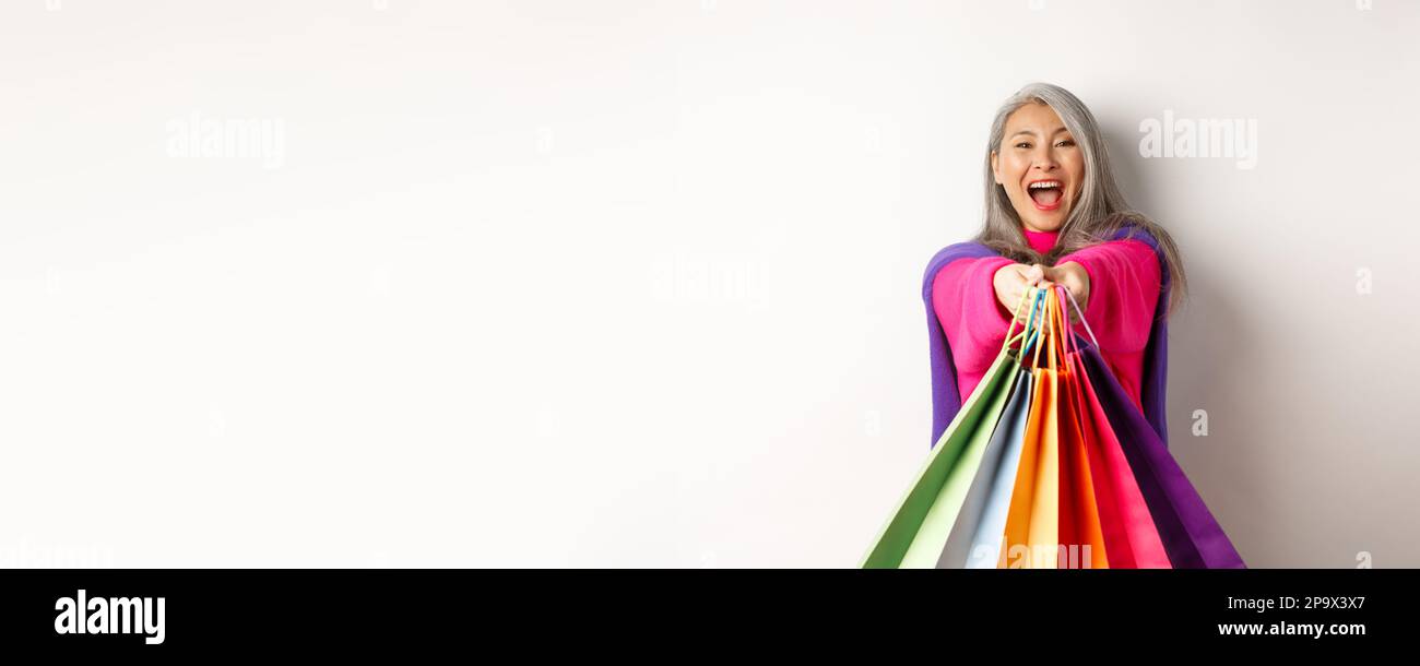 Excited korean lady with grey hair, laughing and showing shopping bags ...