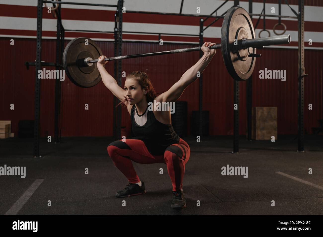 Strong sports woman doing squats with heavy barbell overhead at the crossfit gym. Female ...