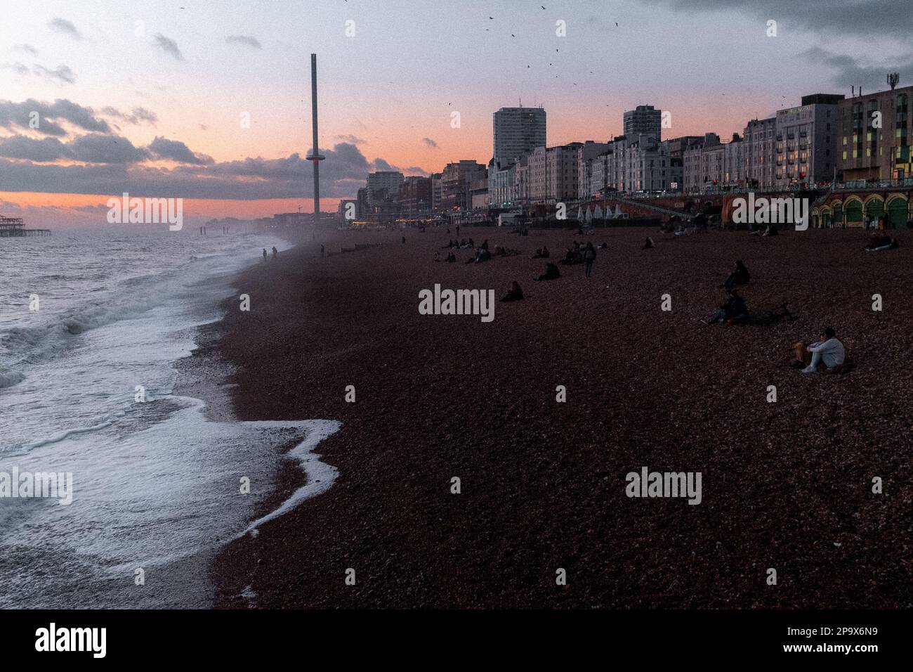 Brighton Beach Sunset in Winter. Lots of people gathered on the pebbles ...