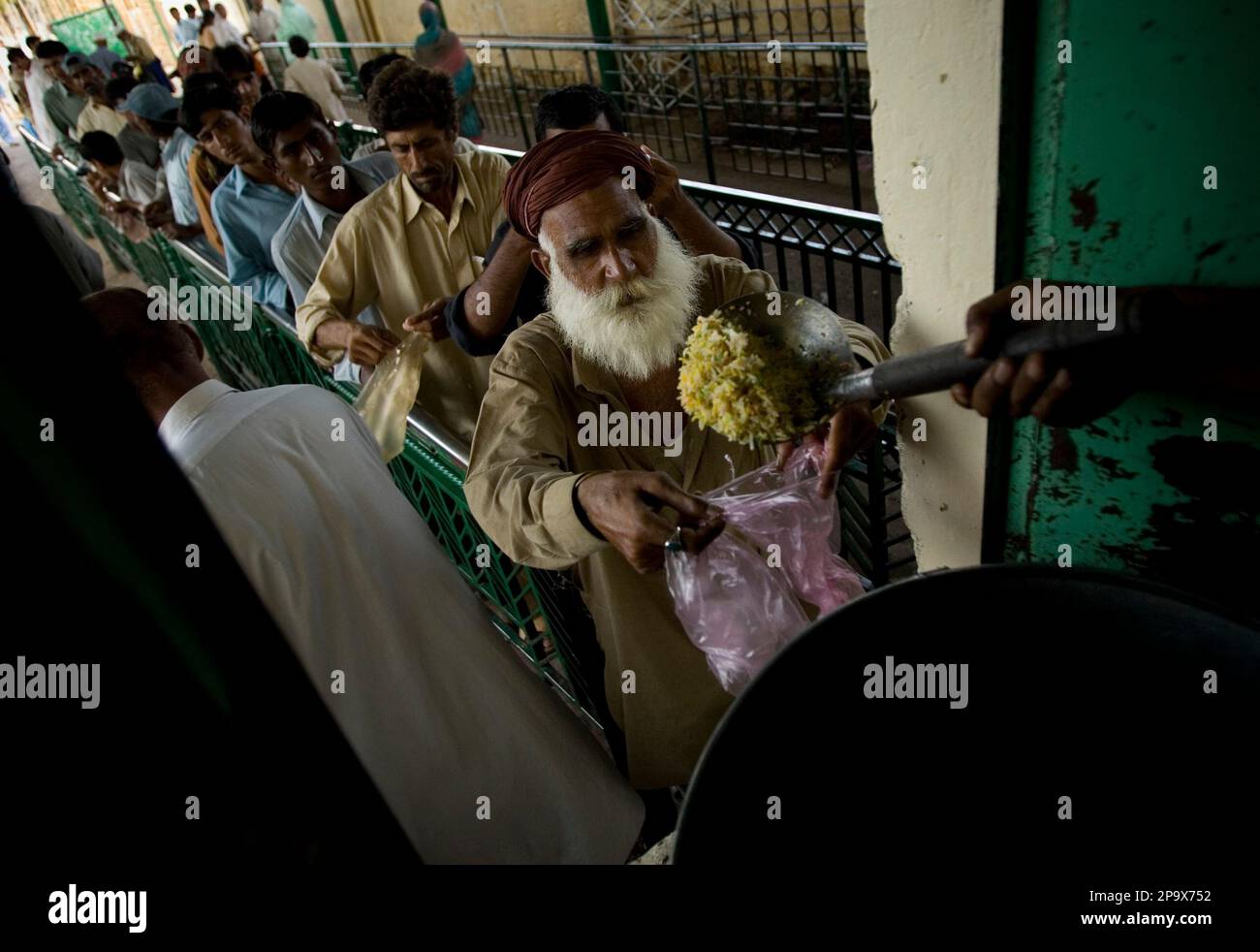 Pakistani men line up as the wait for their donated rice ration during ...