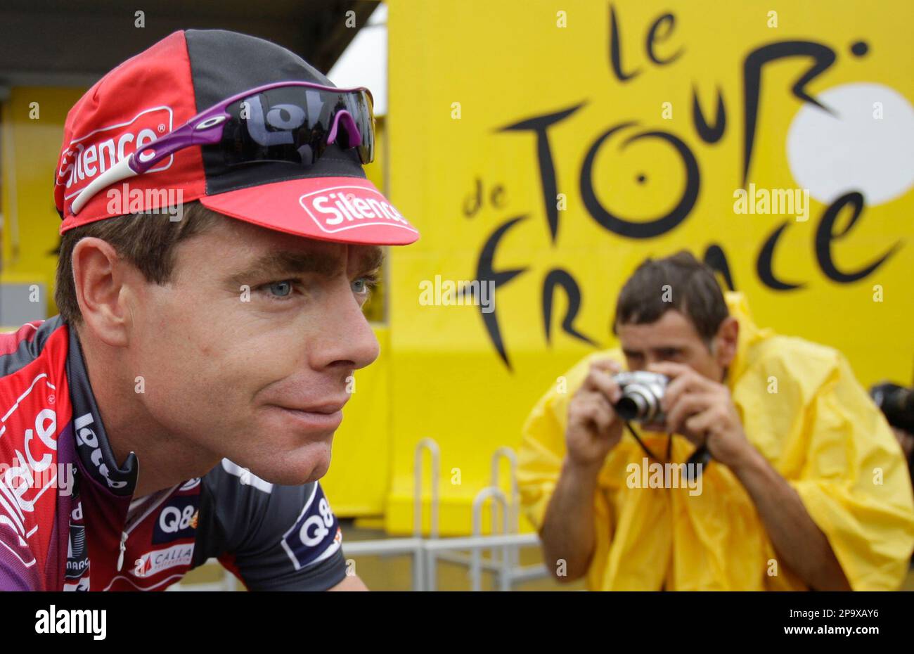 A cycling fan in a rain poncho takes a picture of Cadel Evans of ...