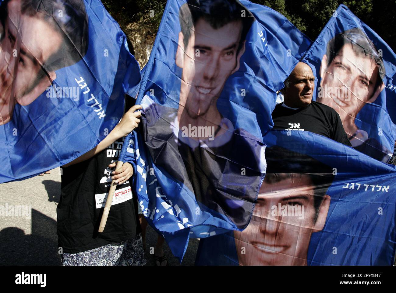 Israelis hold flags showing the photo of captured soldier Eldad Regev ...