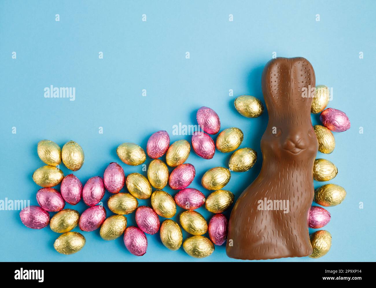 Big milk chocolate bunny and pile of Easter candy eggs foil wrapped in ...