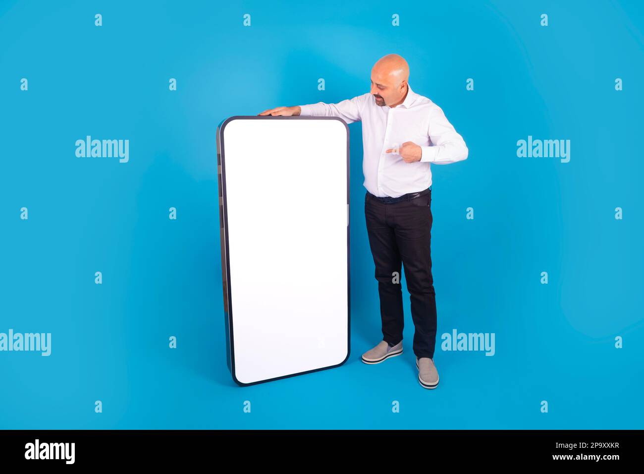Full body length man pointing huge smartphone. Blue studio background ...