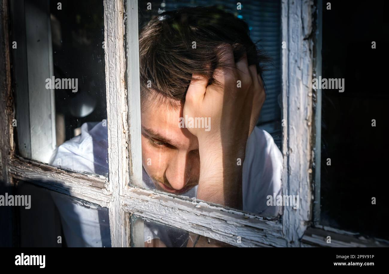 Sorrowful Young Man in the House behind the Old Window Stock Photo - Alamy