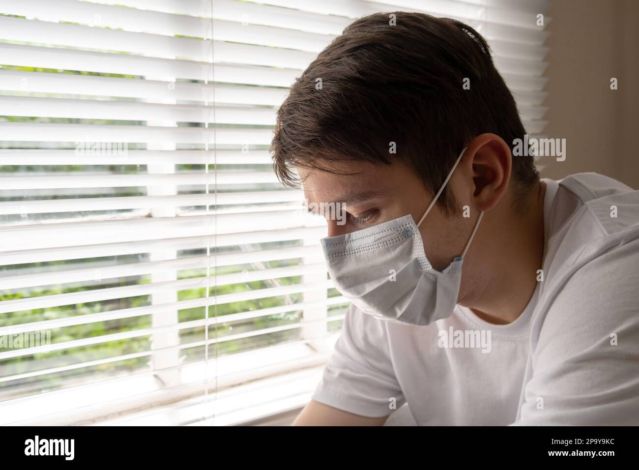 Sad Young Man in a Surgical Mask by the Window in the Room Stock Photo ...