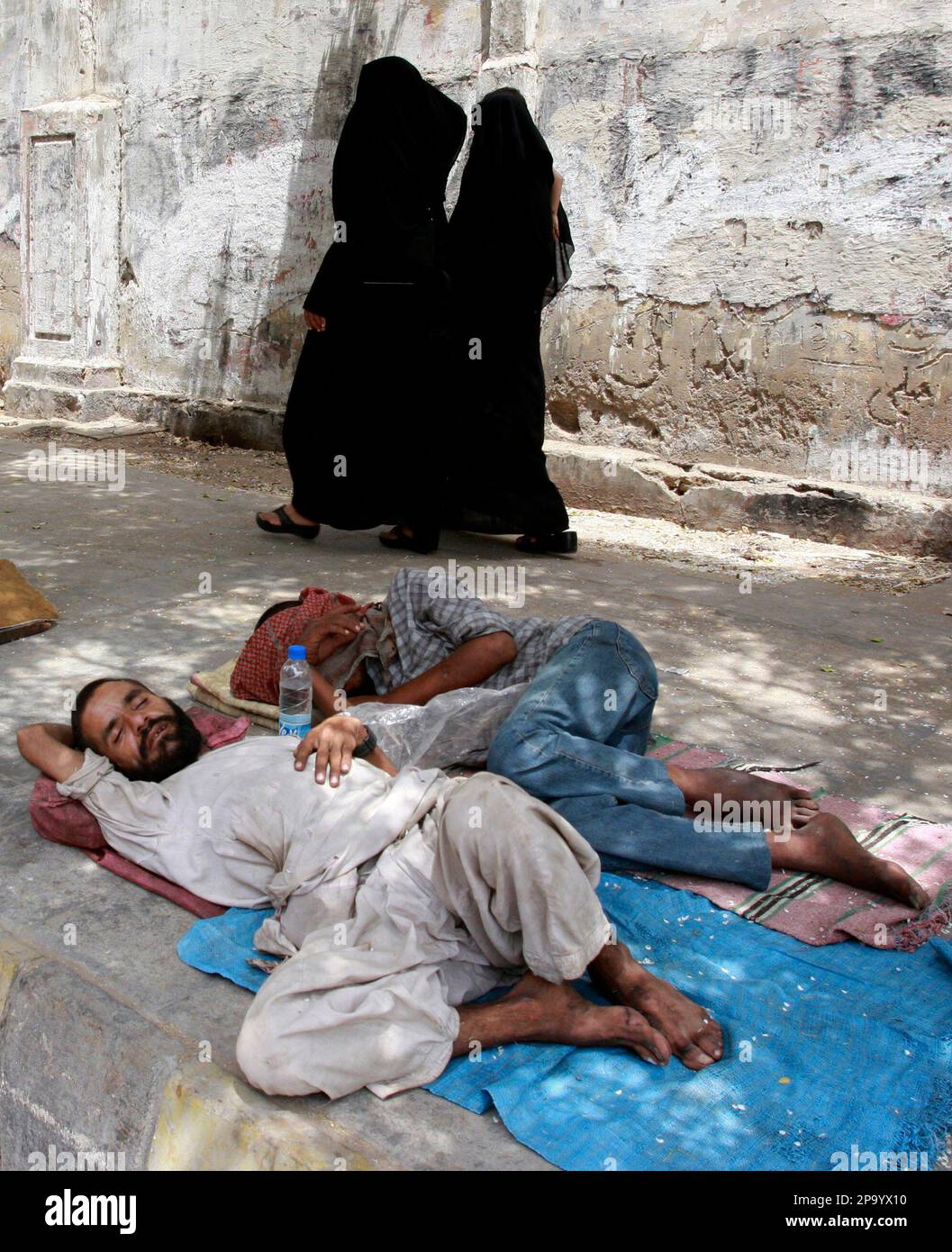 Pakistani women walk past drug addicts napping on a roadside in Karachi ...