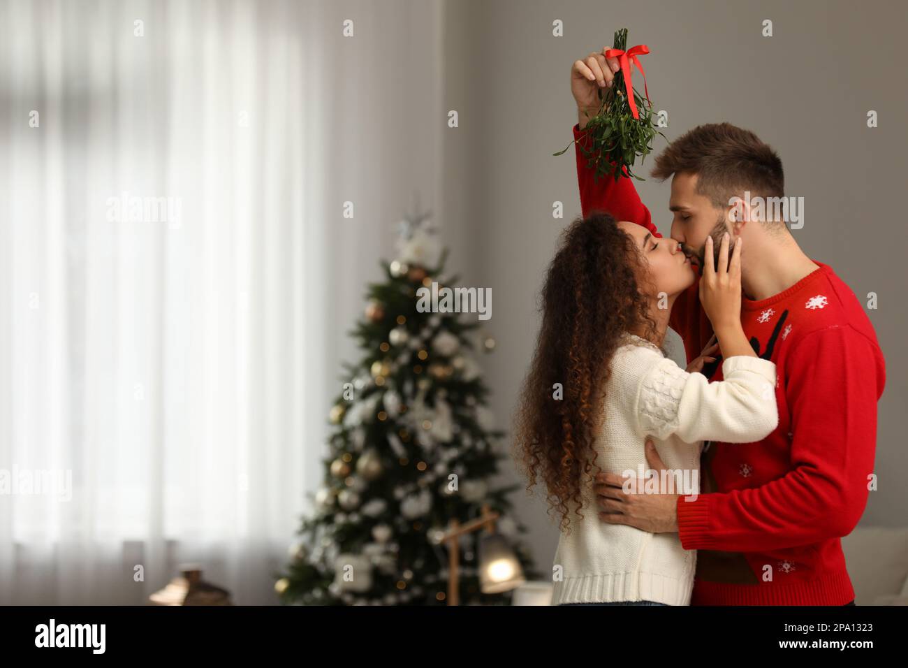 Happy couple kissing under mistletoe bunch in room decorated for Christmas Stock Photo - Alamy