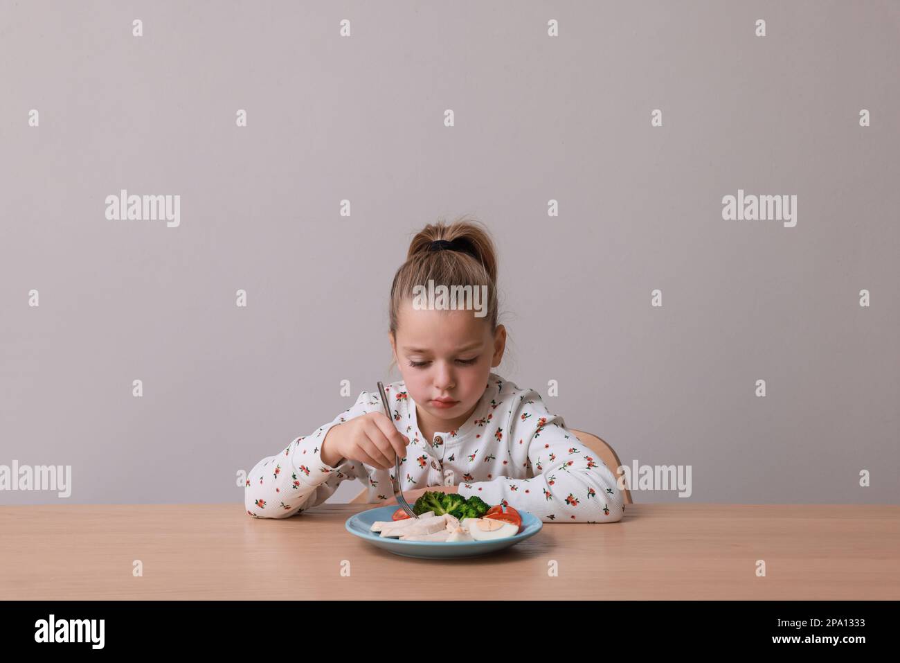 Cute little girl refusing to eat her dinner at table on grey background ...