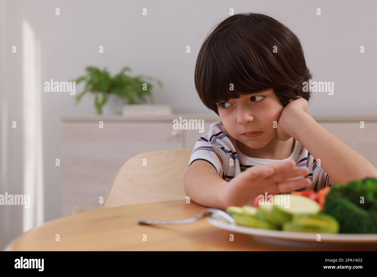 Cute little boy refusing to eat vegetables at home, space for text ...