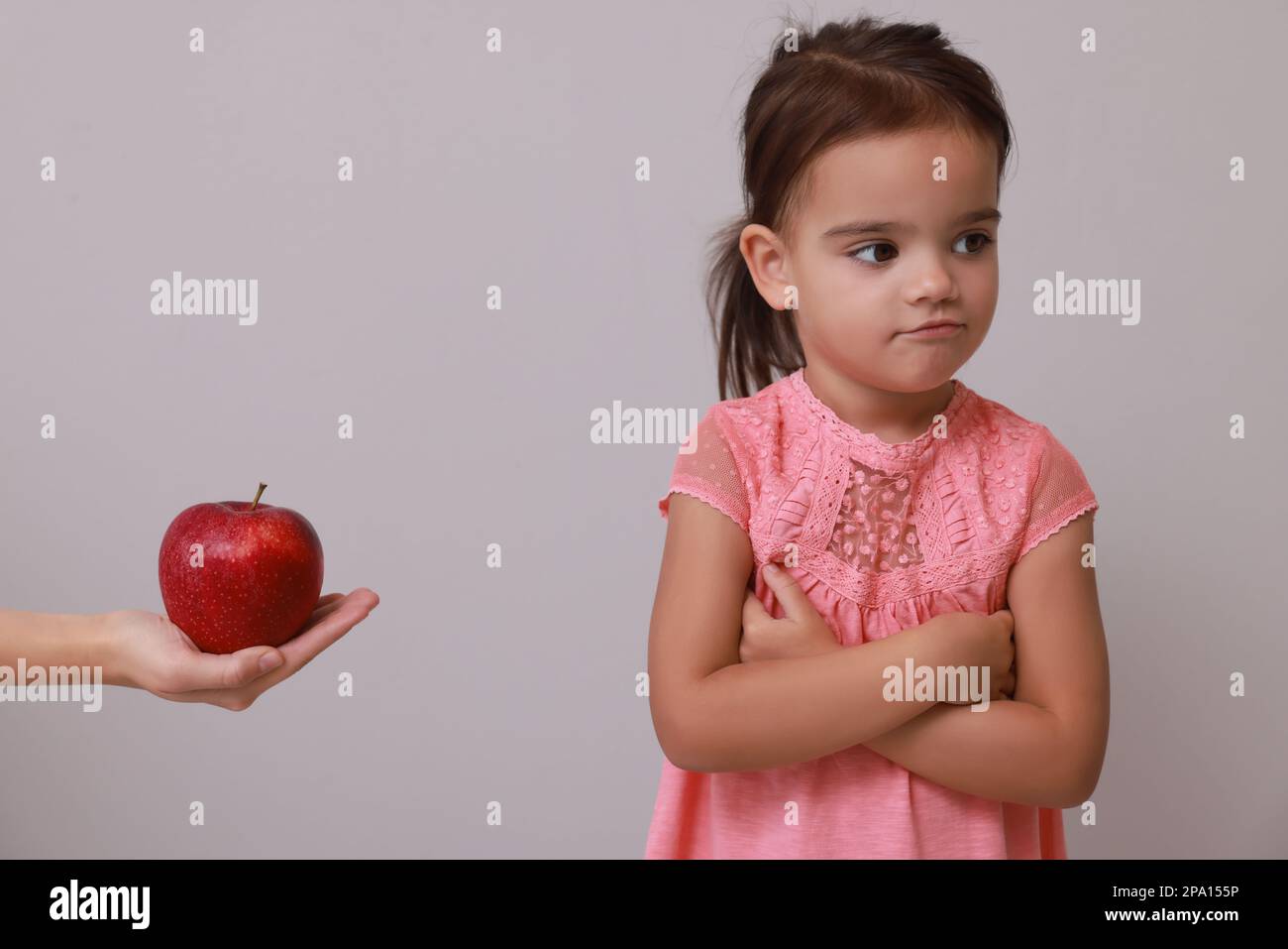 Cute little girl refusing to eat apple on grey background Stock Photo ...
