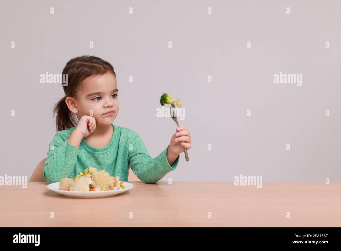 Cute little girl refusing to eat vegetable salad at table on grey ...
