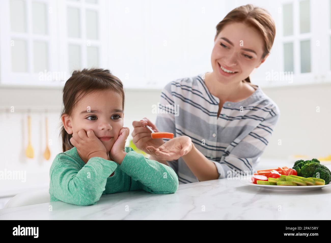 Mother feeding her daughter in kitchen. Little girl refusing to eat ...