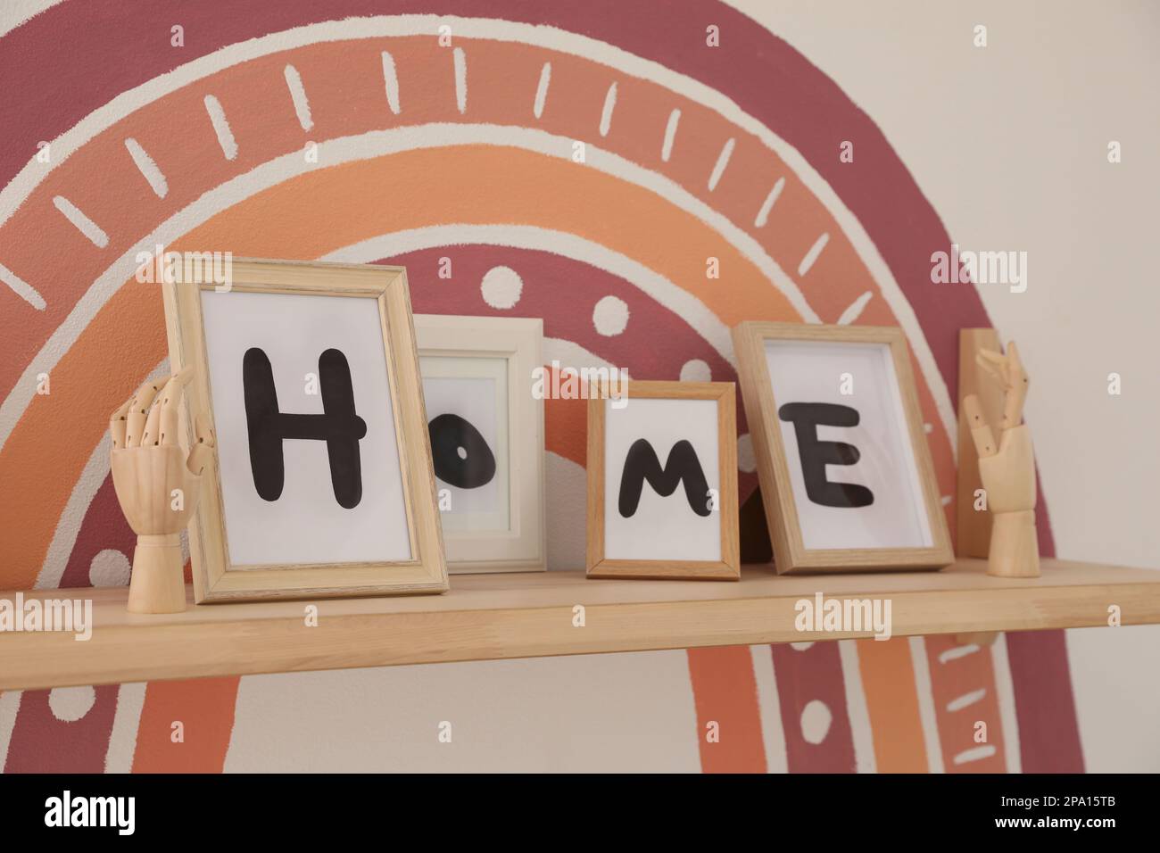 Wooden shelf with word HOME and rainbow on white wall indoors. Interior ...