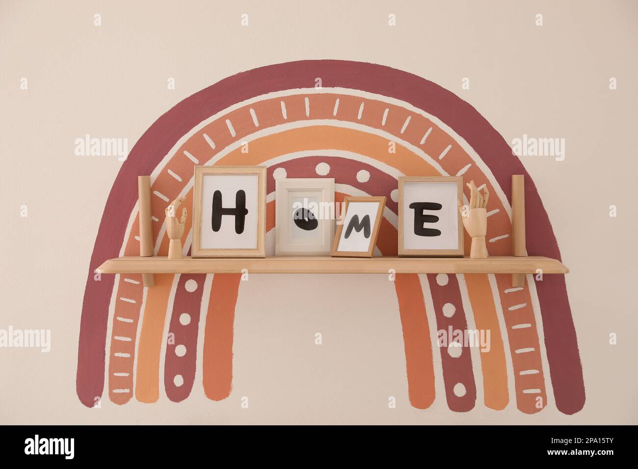 Wooden shelf with word HOME and rainbow on white wall indoors. Interior ...